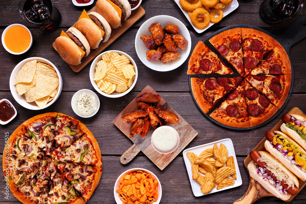 Junk food table scene. Pizza, hamburgers, hot dogs, chicken wings and ...