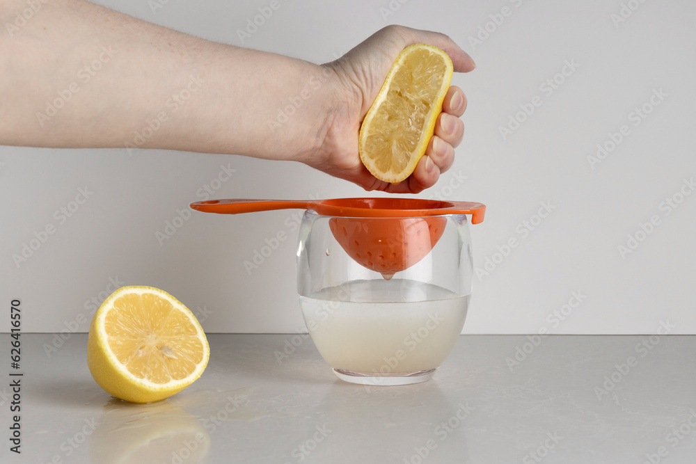 making lemon water, hand squeezes a half lemon over a strainer on a ...