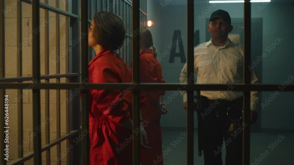 Two female prisoners, inmates in orange uniforms stand facing the metal ...