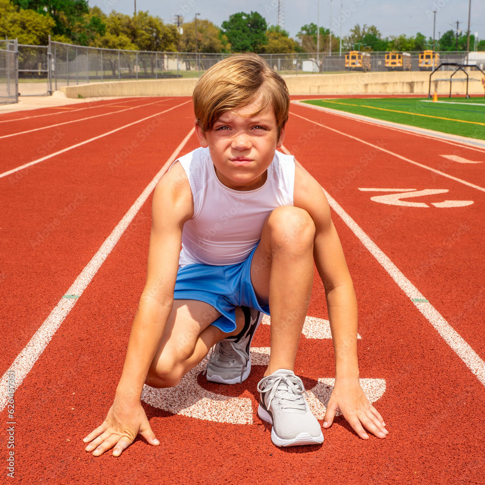 Preteen male track runner with heads up in kneeling stance ready to run ...