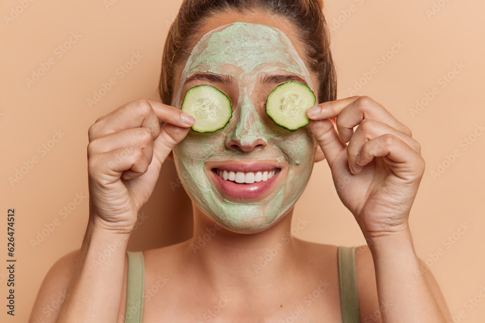 Young dark haired European woman indulges in soothing ritual of applying facial clay clay mask ...