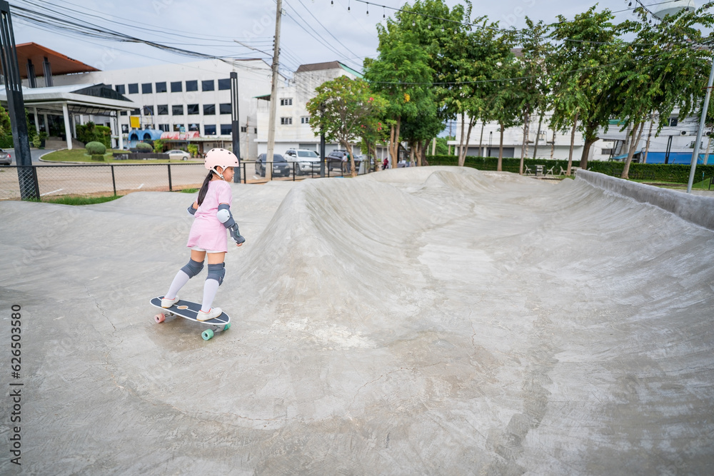 asian child skater or kid girl playing skateboard or ride surf skate and fun in pump track snake ...