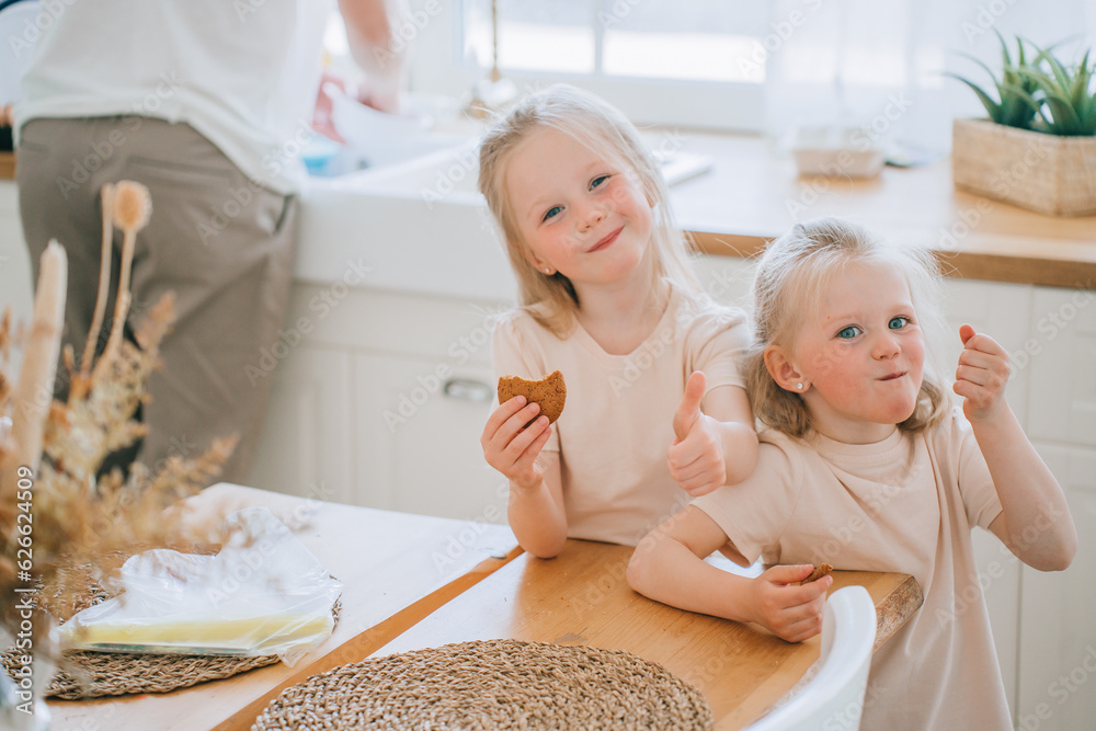 Cheerful caucasian little girls eating cookies at kitchen while father ...