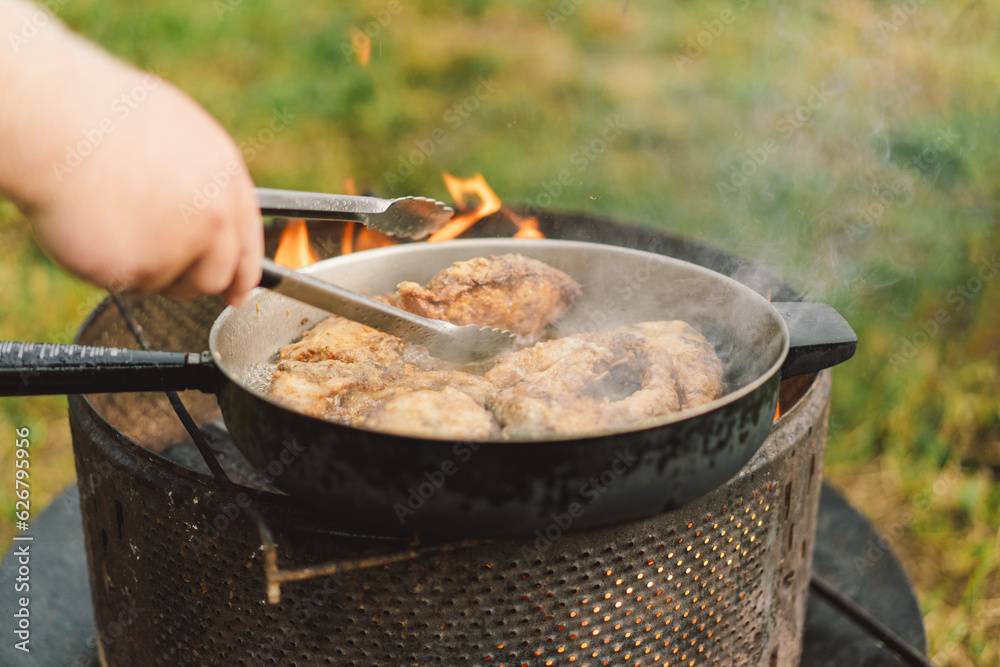 Cooking in the woods outdoors. Man cooking fish on fire in rainy ...