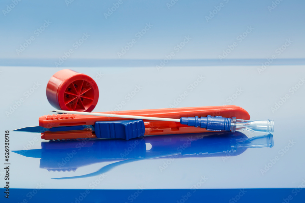 Red safety scalpel, filter needle and red locking disposal cup on blue ...