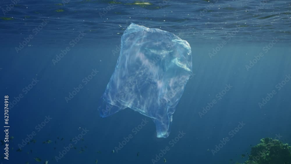 Disposable blue plastic bag floating in blue water in bright sunrays ...