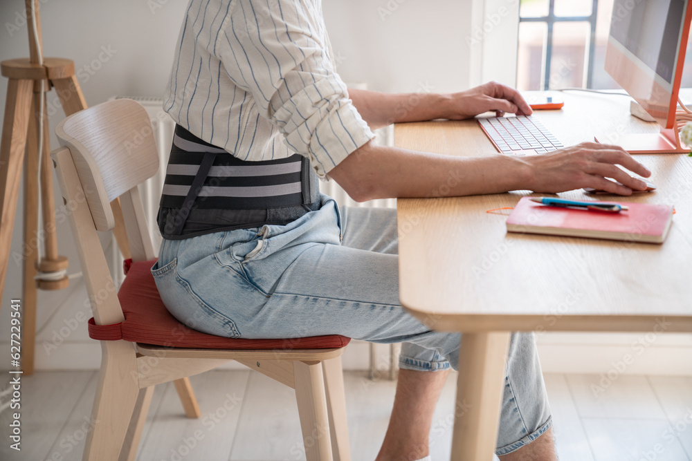 Freelancer man works types on computer keyboard wears back support belt ...