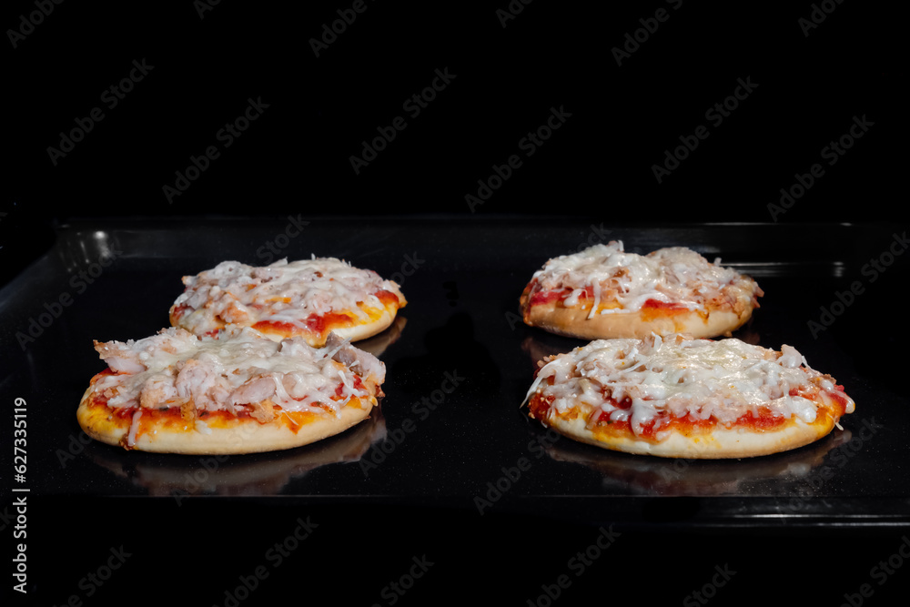 Four baked mini pizzas with ham, sause, cheese on tray in electric oven ...
