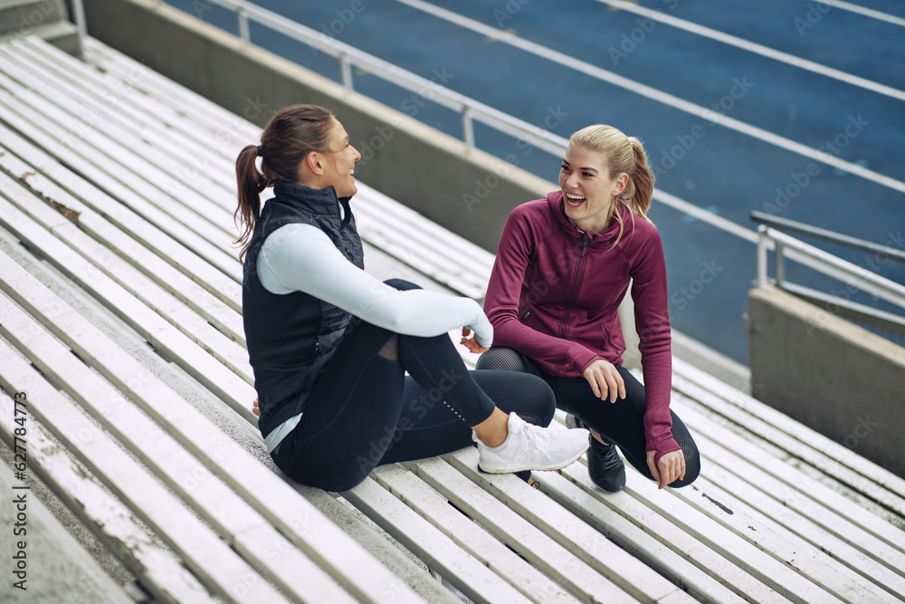 Two laughing women sitting on running track bleachers together after a ...