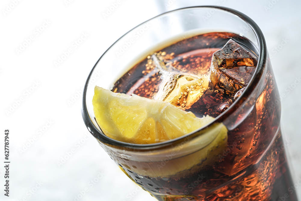 Part of a drinking glass with fresh cola, ice cubes and lemon slice, refreshing sweet caffeine ...