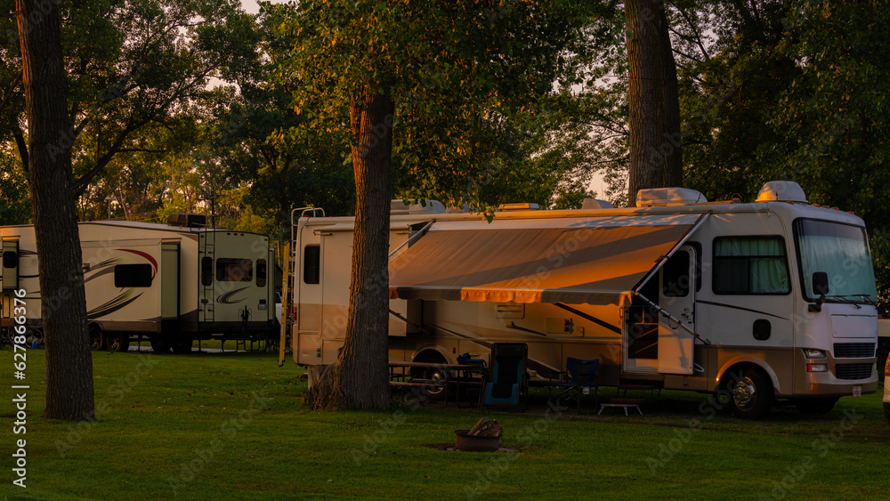 Rv and trailers parked at campsites amongst tall trees in early morning ...