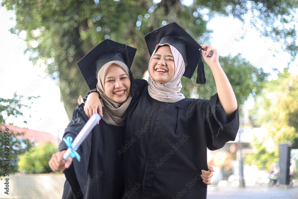 Two young muslim ladies in graduation costumes posing at camera at ...