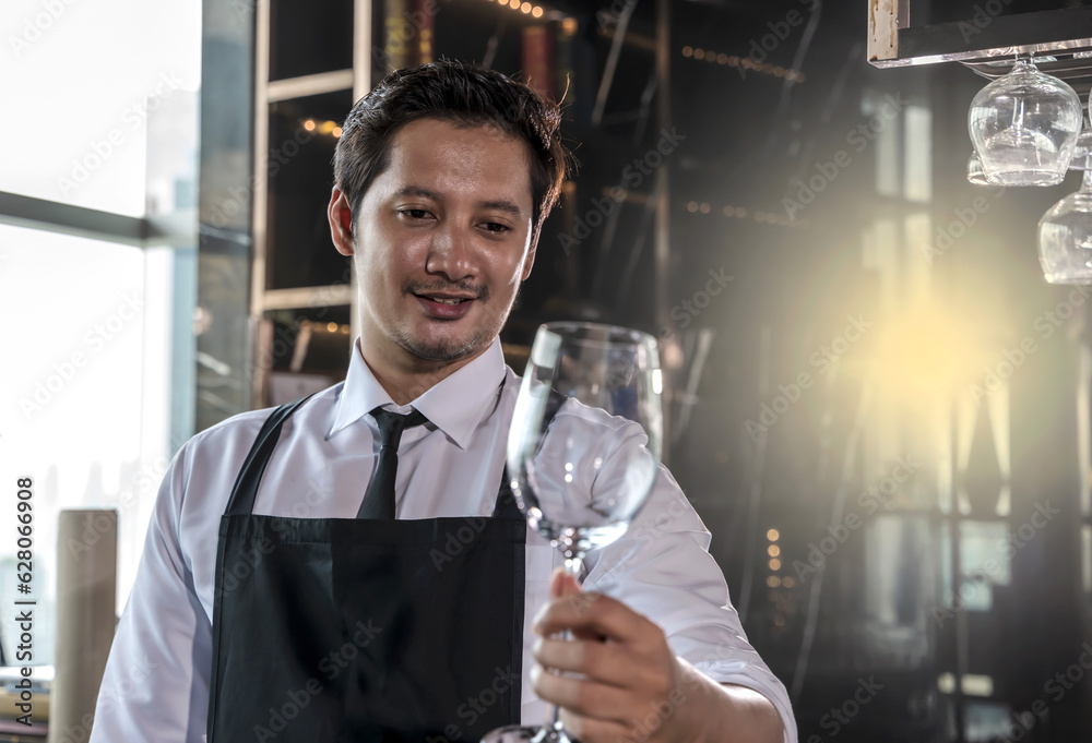 Young Asian bartender man holding empty wine glass checking clean in ...