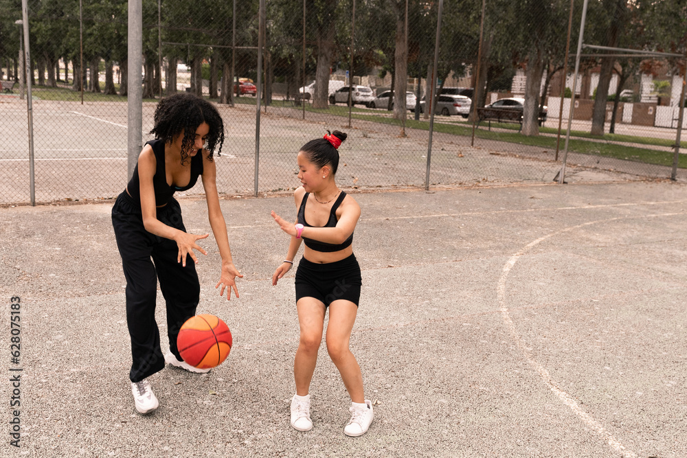 Chinese girl with black hair plays basketball with her Latina friend on ...