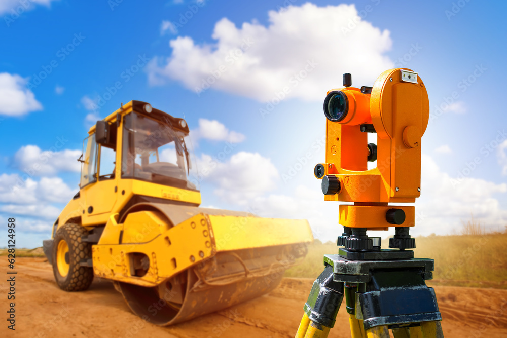Road construction. Geodetic instrument. Asphalt roller on dirt road ...