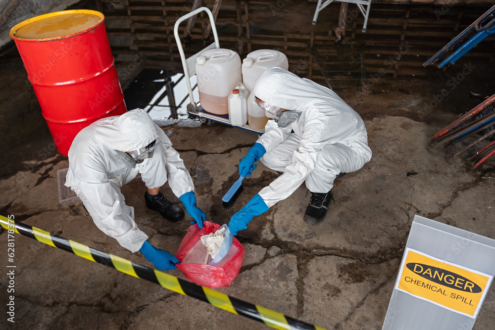 A team of two chemists, wearing PPE suits and gas masks, recover a ...