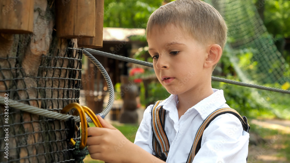 Little boy adjusting safety rope and hook in rope adventure park ...