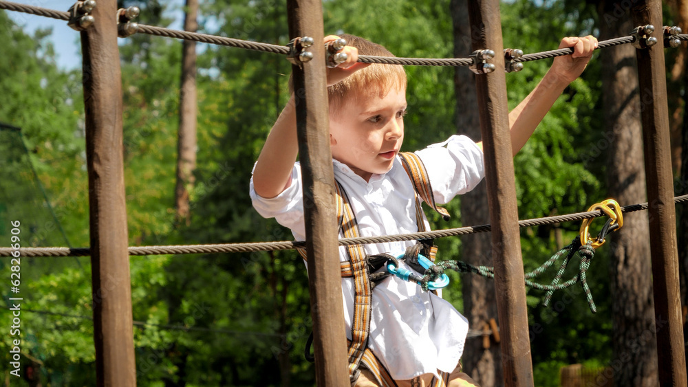 Portrait of little boy climbing over obstacles while having fun in rope ...
