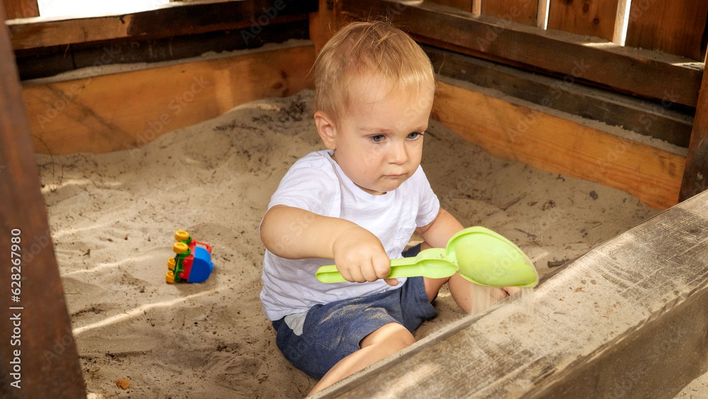 Little baby boy playing in wooden sandbox and digging sand with shovel ...