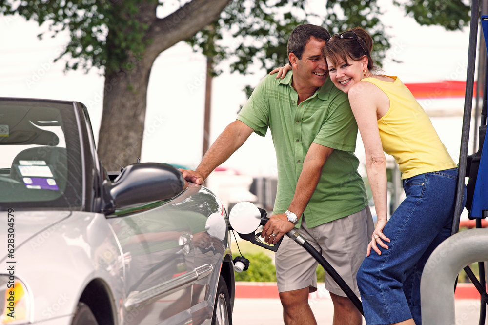 Foto de Flirty older couple pumping gas into convertible car at gas ...