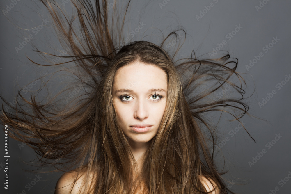 brunette girl with flowing hair in the air studio portrait against gray ...