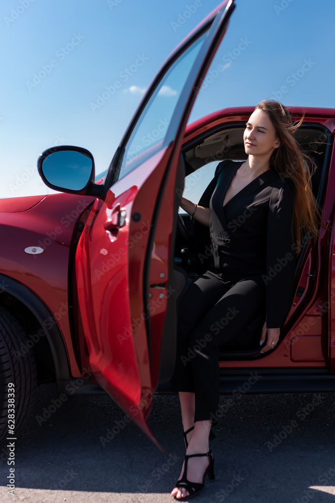 Beautiful girl in a black suit and high heels sits behind the wheel in ...