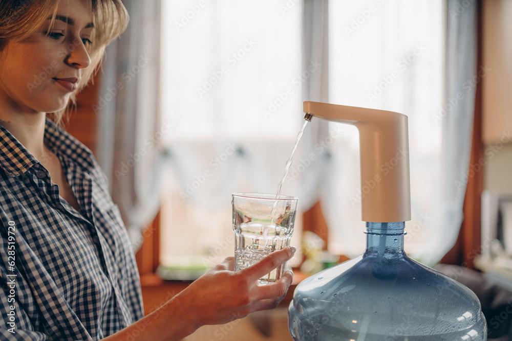 Woman's hands pour water into glass from an automatic water cooler ...