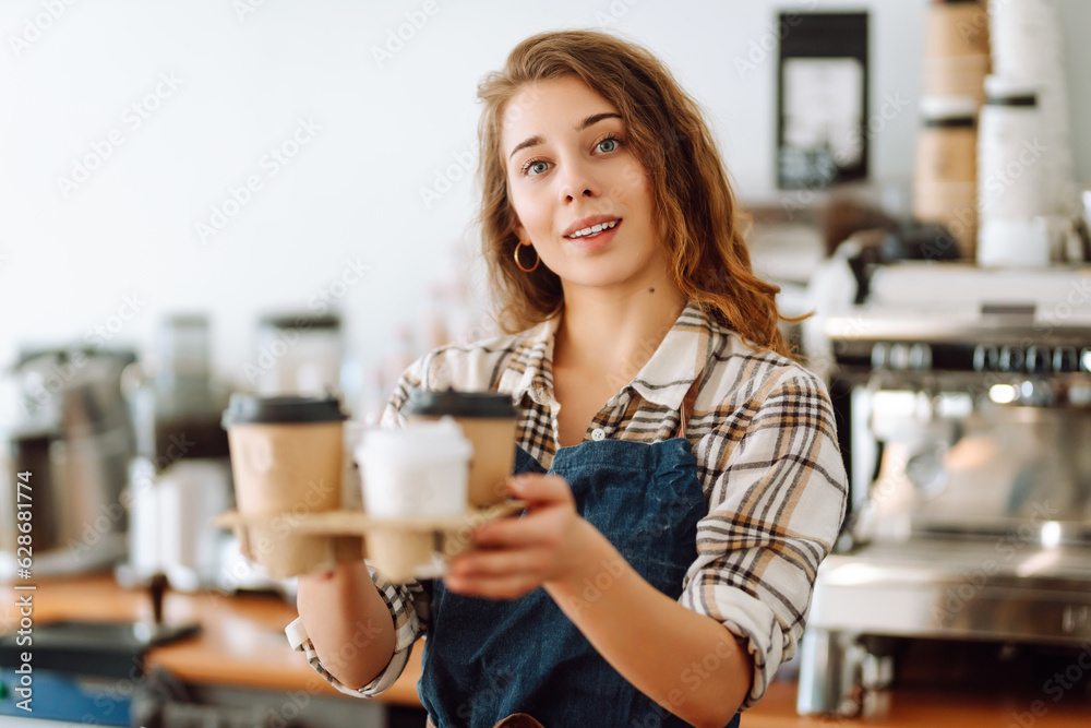 Portrait of a young woman barista holding takeaway coffee in her hands ...
