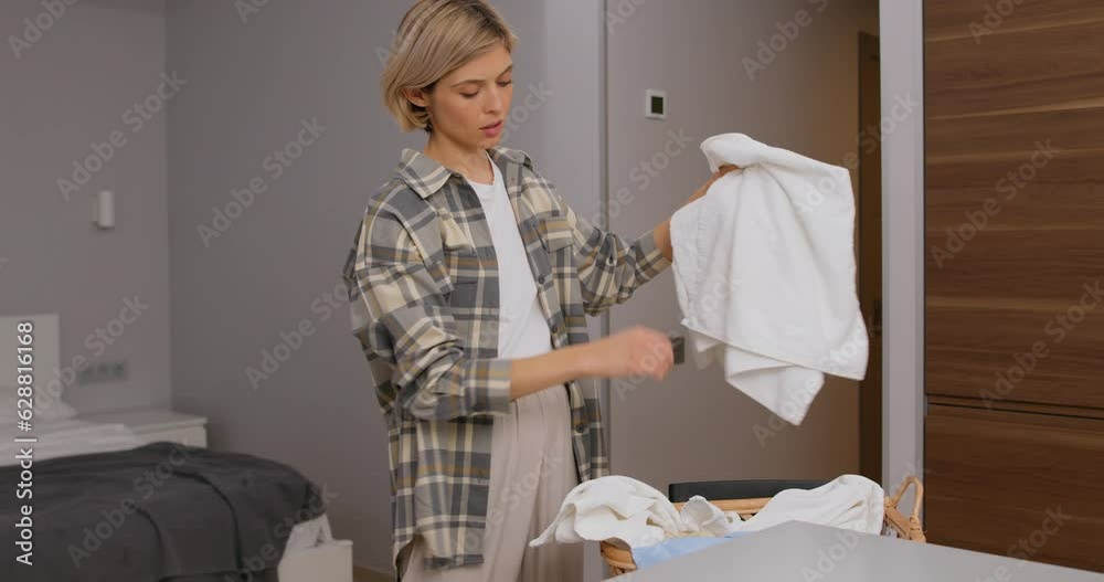 Young beautiful woman is sorting clean washed white clothes, taking ...