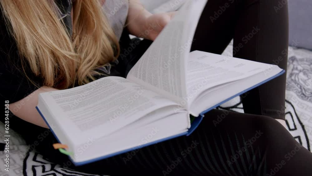 Girl with long blond hair sitting on the bed and reading a thick book ...