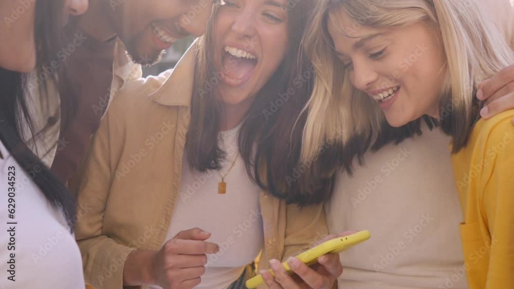 Young group of millennial people having fun using cell phone together outside. Cheerful ...