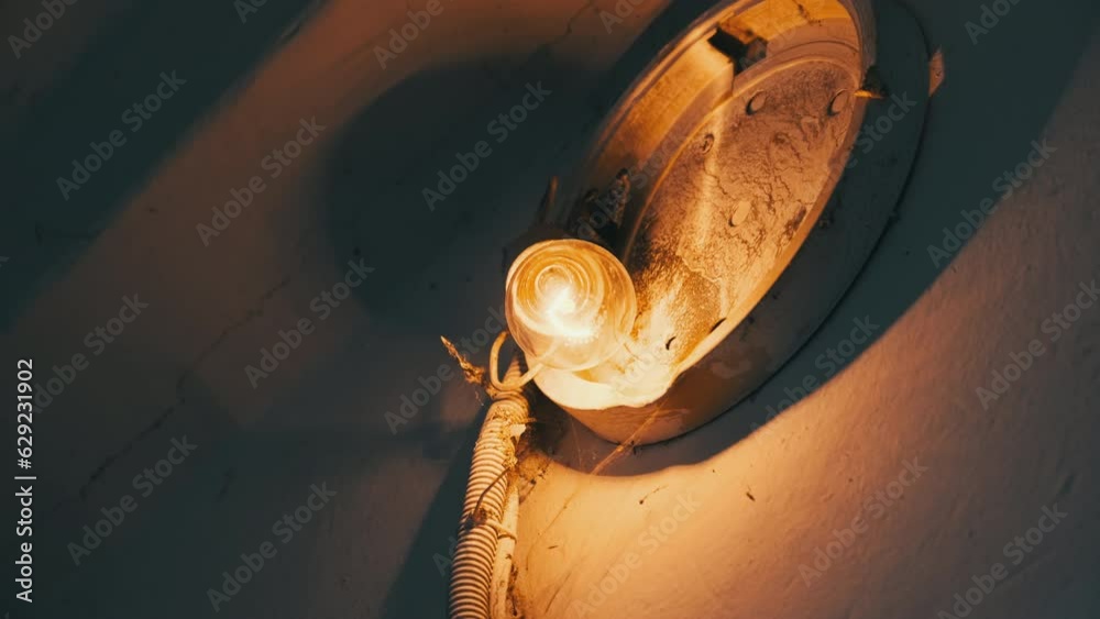 An old incandescent light bulb glows on a broken lamp on the concrete ...