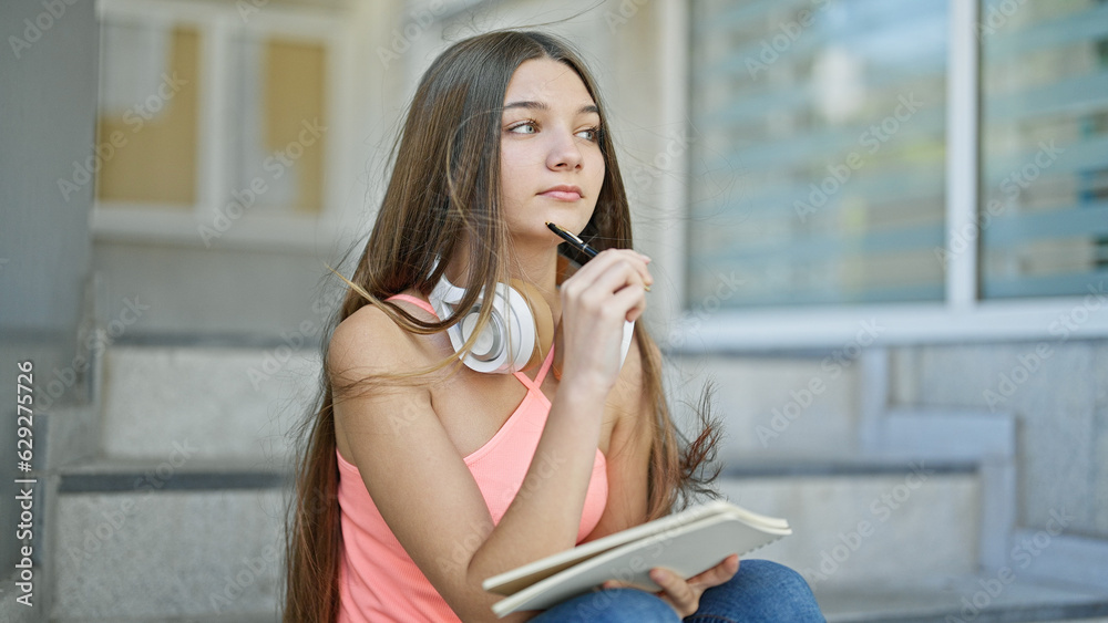 Young beautiful girl student taking notes sitting on stairs thinking at ...