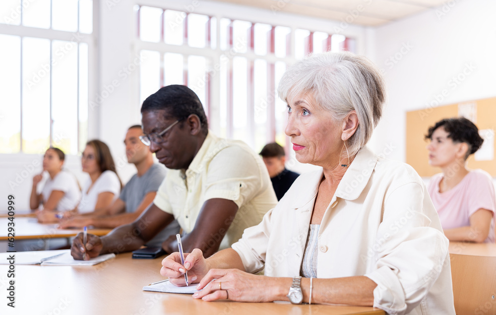 Positive interested elderly woman listening attentively and taking ...