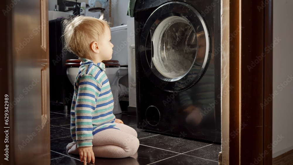 Little baby boy looking with interest on spinning drum of washing ...
