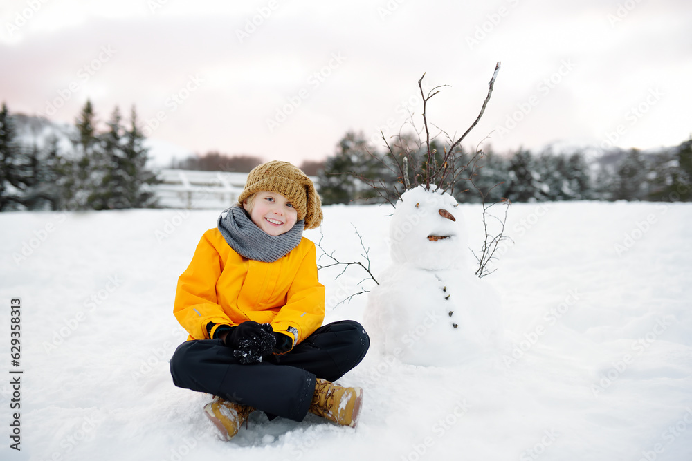 Preteen boy builds funny snowman in snowy park. Happy child having fun ...