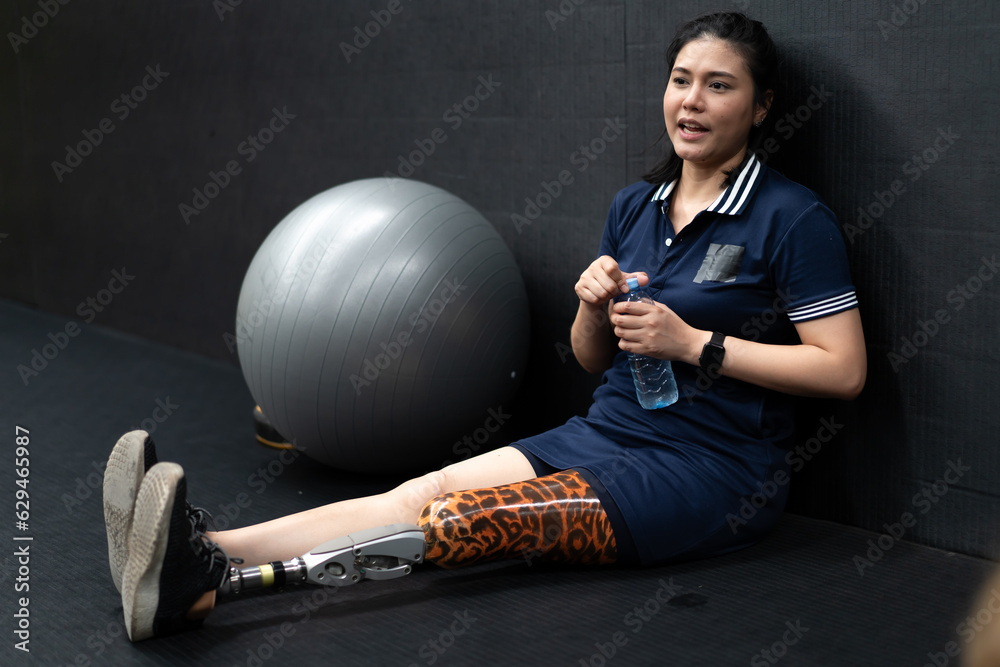Asian woman with prosthetic leg sits isolated in gym. Young girl with ...