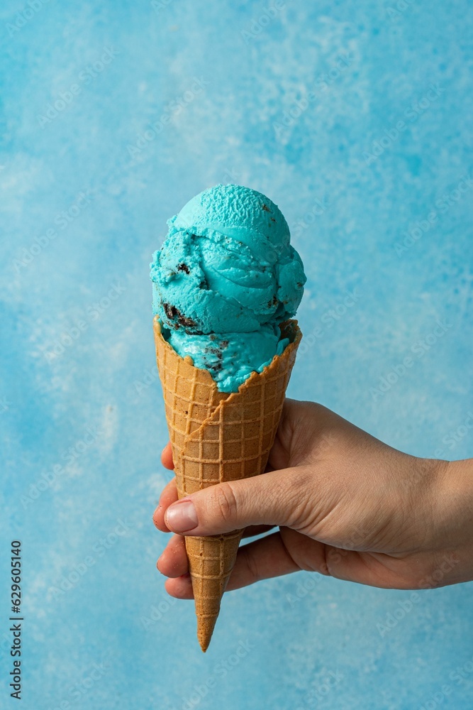 Hand holding two scoops of blue ice cream cone against a blue ...