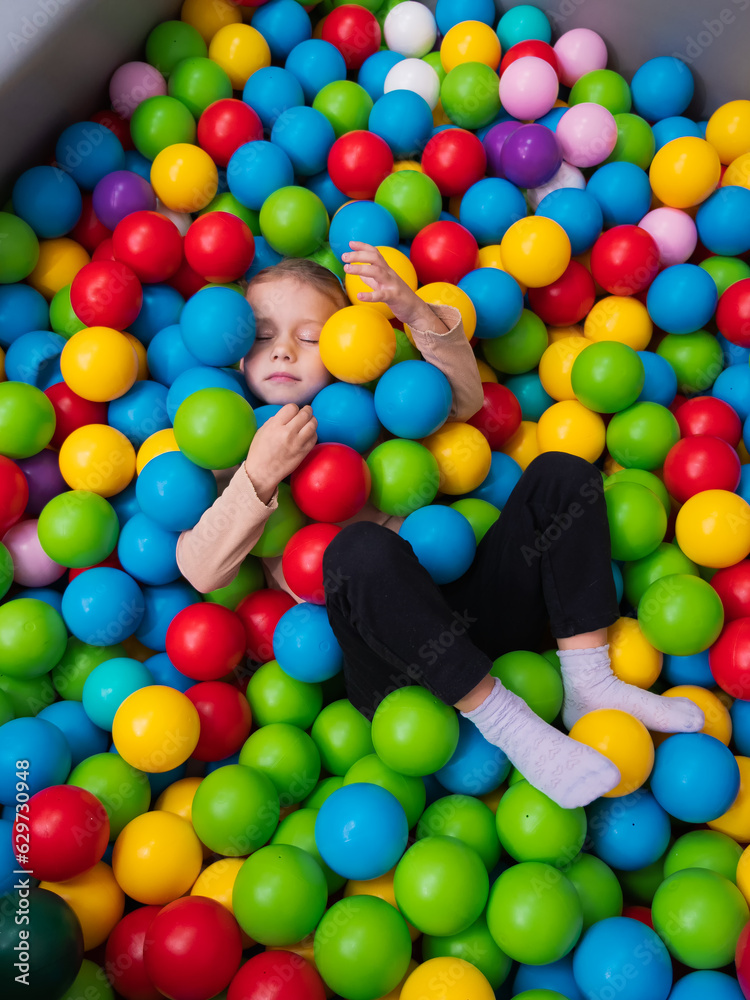 Cute little girl playing on multi coloured plastic balls in big dry ...