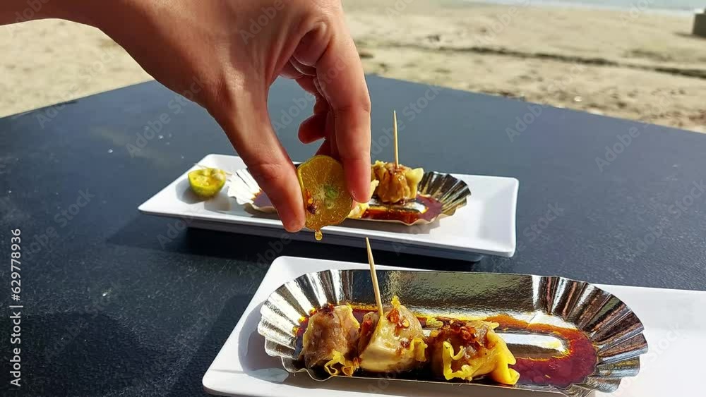 Hand squeezing calamansi juice over pork siomai, a traditional Filipino ...