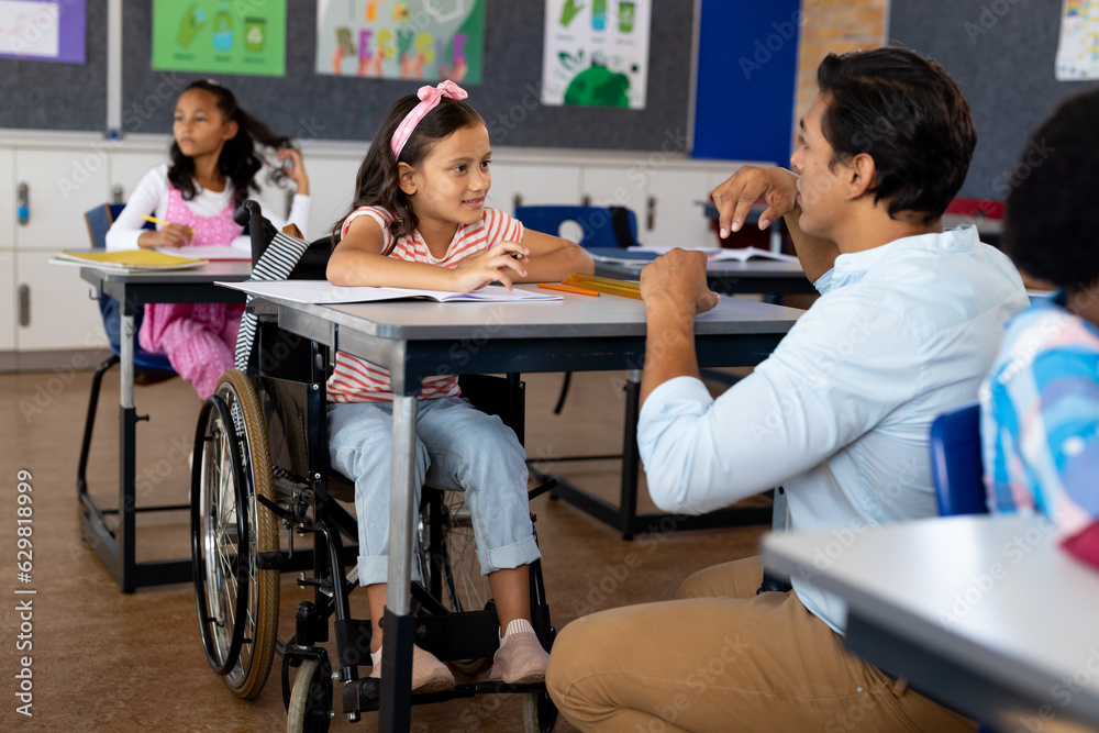 Happy biracial male teacher with girl in wheelchair in class at ...