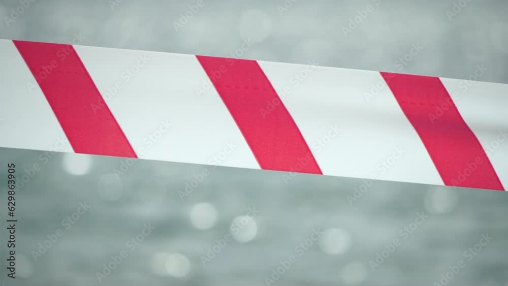 Red white warning tape barrier ribbon swinging in the wind across ...