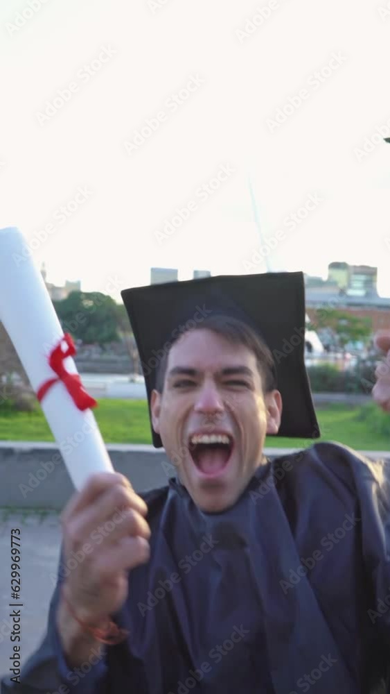 Happy graduated man in a black gown showing his diploma to the camera ...