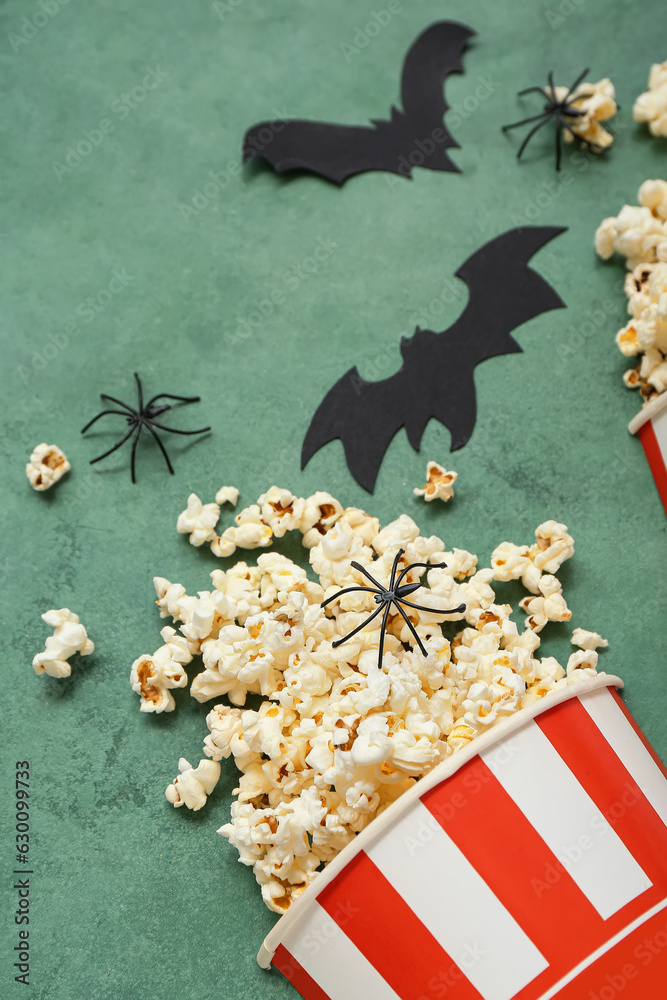 Bucket with tasty popcorn, spiders and paper bats on green background ...