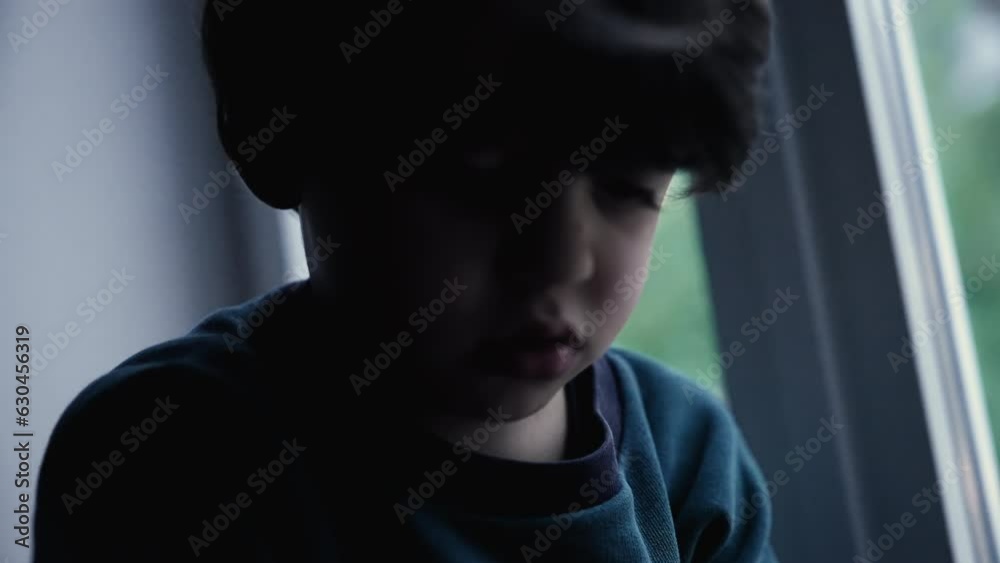 Sad depressed child sitting by window in the dark, gloomy moody ...