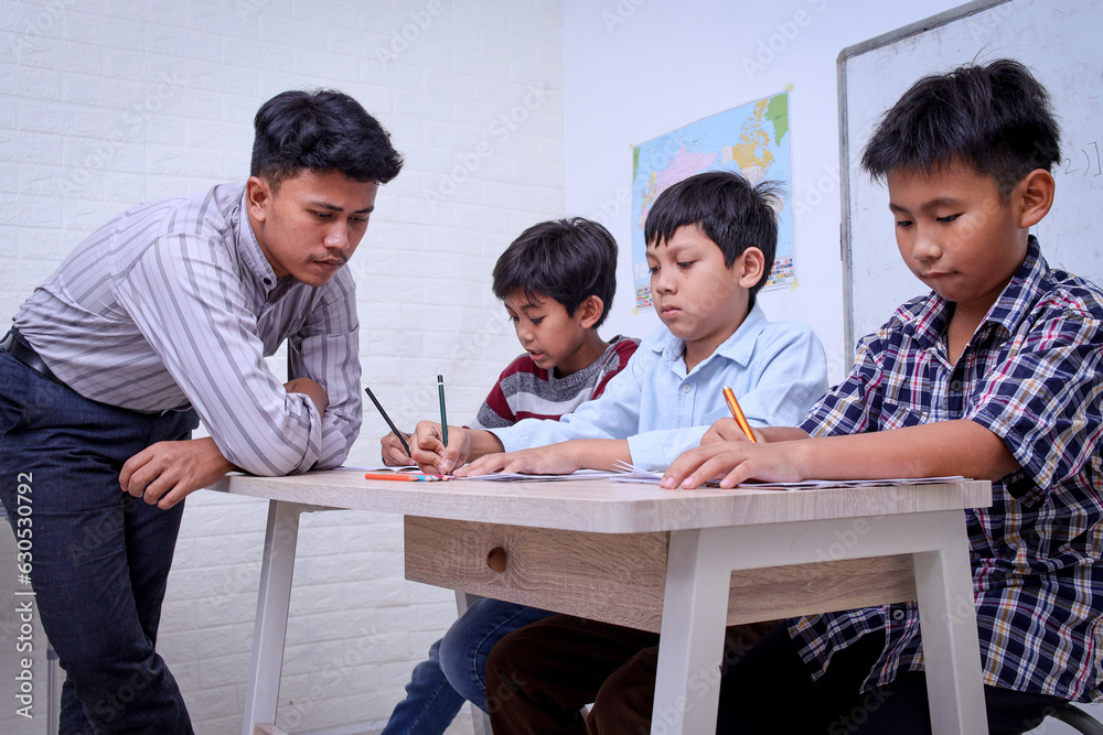 Asian male school teacher checking the students writing tasks in ...