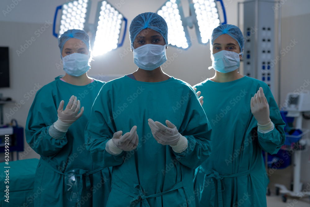 Portrait of diverse female surgeons wearing surgical gowns in operating ...