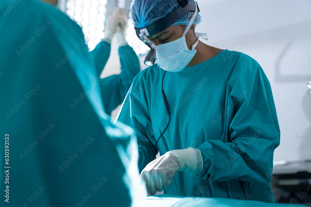 Diverse surgeons wearing surgical gowns operating on patient in ...