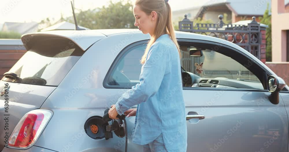 Close-up. Woman plugs in charger into socket of her modern new electric ...