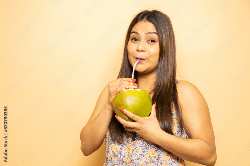 Young beautiful indian woman drinking coconut water isolated on beige ...